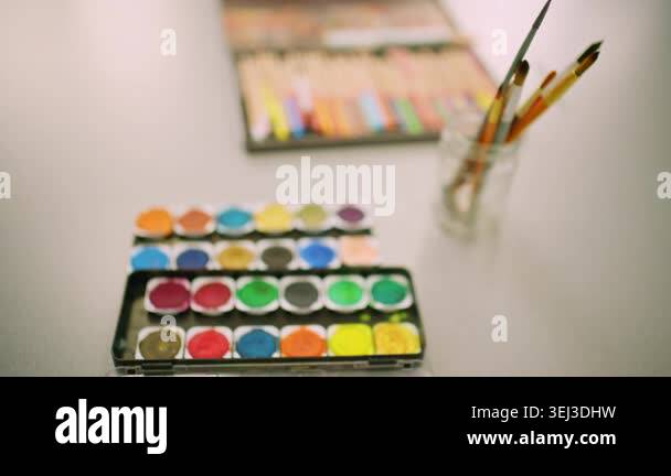 Close up of paintbrushes in a glass jar with watercolor palette and ...