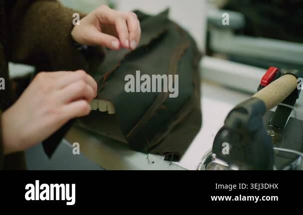 Close up of a tailor using a professional steam iron on black fabric in ...