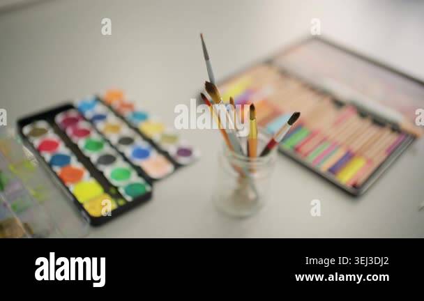 Close up of paintbrushes in a glass jar with watercolor palette and ...