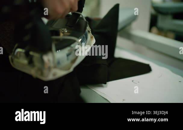 Close up of a tailor using a professional steam iron on black fabric in ...