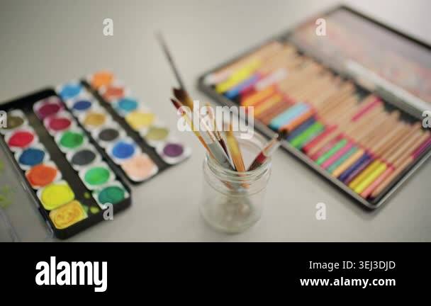 Close up of paintbrushes in a glass jar with watercolor palette and ...