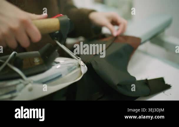 Close up of a tailor using a professional steam iron on black fabric in ...
