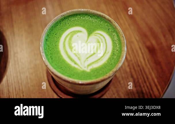 Top down close up of a matcha latte served in a ceramic cup on a wooden ...