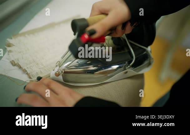 Designer's hands use a professional steam iron to press white fringed ...