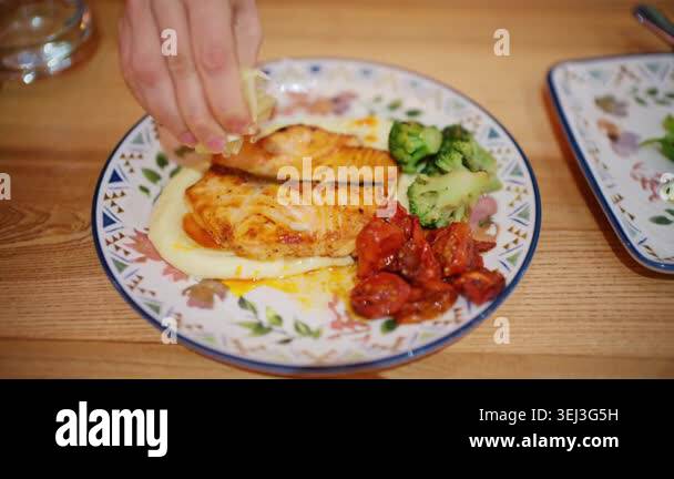 A close up shows a hand squeezing a lemon over a piece of grilled ...