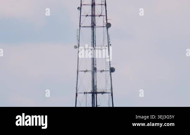 A tall metal telecommunications tower stands against a pale sky ...