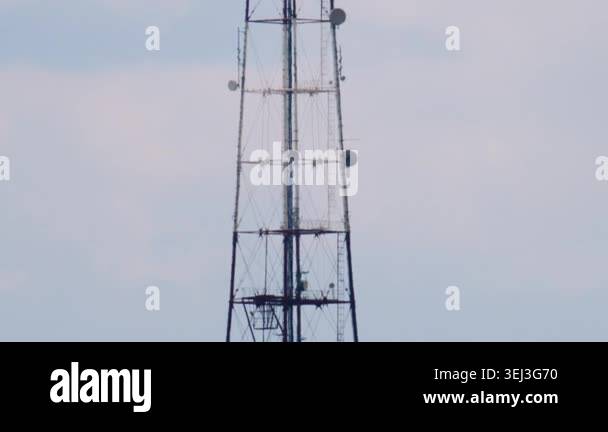 A tall metal telecommunications tower stands against a pale sky ...