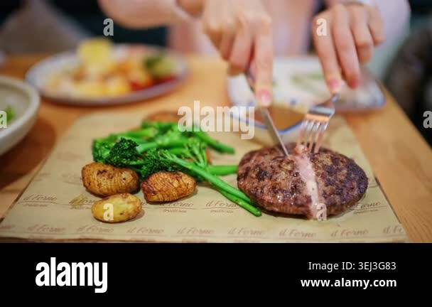 A cooked burger patty is being cut on a serving board alongside ...