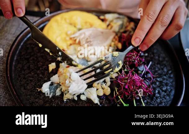 Close up of hands using a fork and knife to cut into a gourmet seared ...