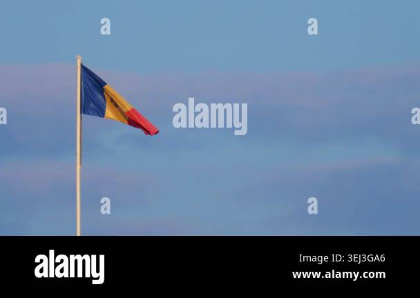 Moldovan national flag waving on a tall flagpole against a clear blue ...