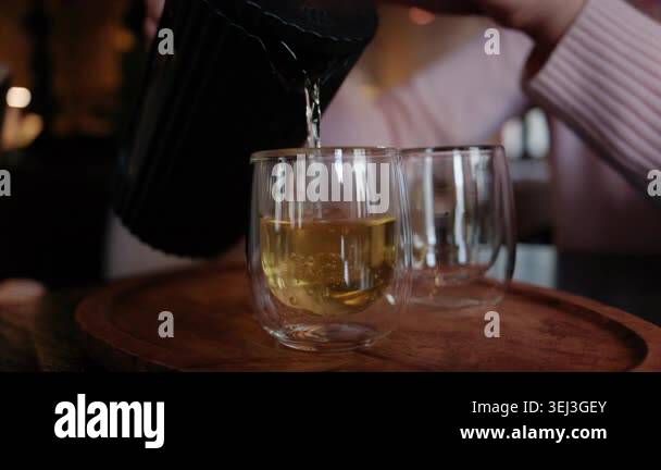 Hot tea being poured from a teapot into a glass cup on a wooden tray ...