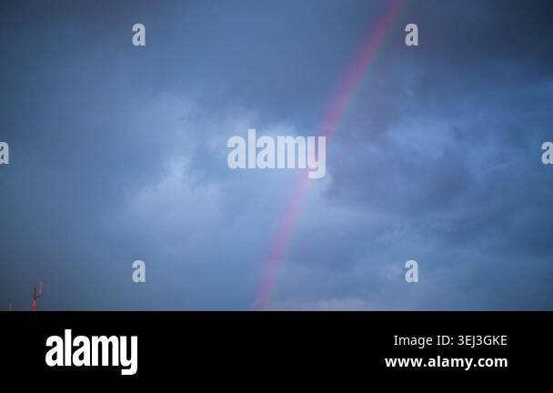 Partial rainbow visible through dense grey storm clouds in the sky ...