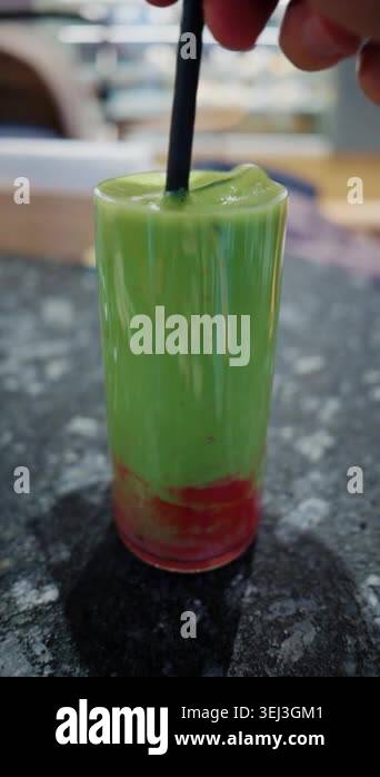 Close up of a colorful green beverage with a black straw on a cafe ...