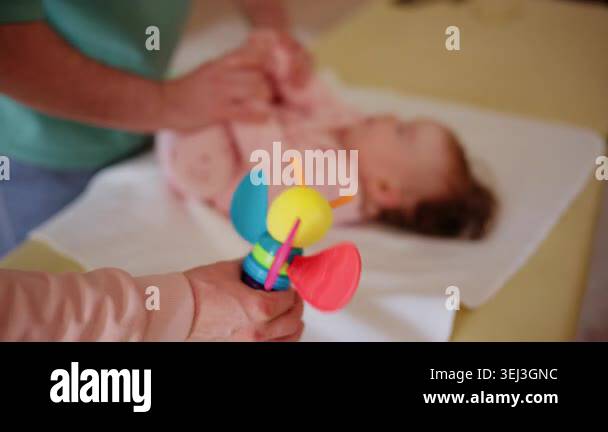 Colorful baby sensory toy in the foreground while an infant receives ...
