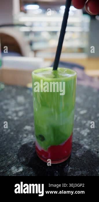 Close up of a colorful green beverage with a black straw on a cafe ...