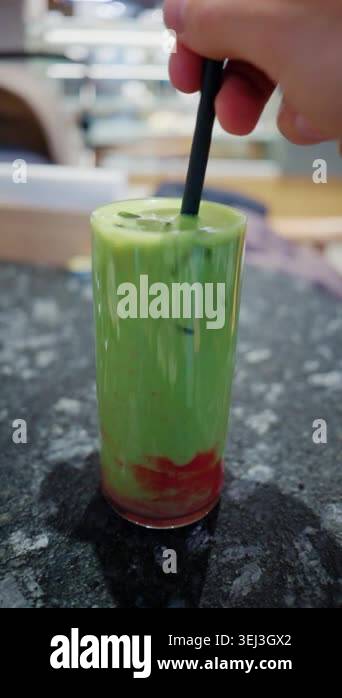 Close up of a colorful green beverage with a black straw on a cafe ...