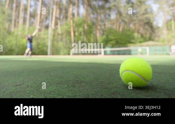 Close-up of a bright yellow tennis ball on green synthetic grass in a ...