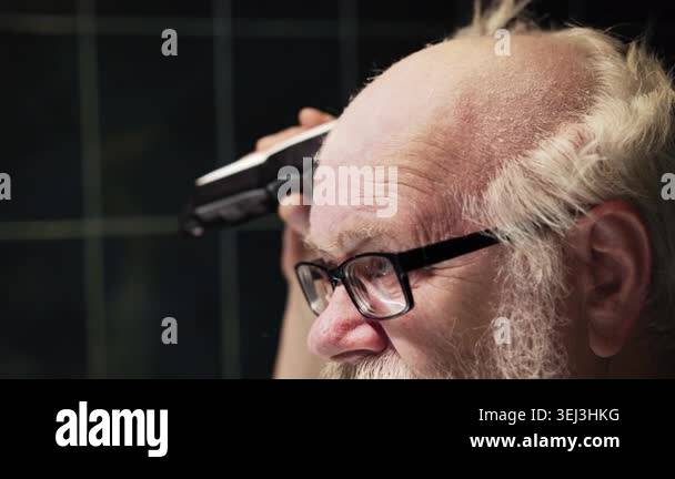 White hair pension man wearing glasses using a trimmer in his hands to ...