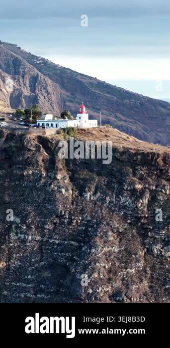 A white lighthouse and buildings stand prominently on towering ocean ...