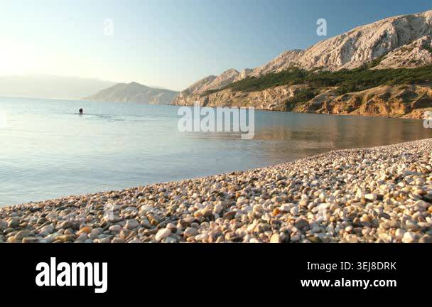 man swimming Calm pebble beach with sea and rocky mountains croatia krk ...