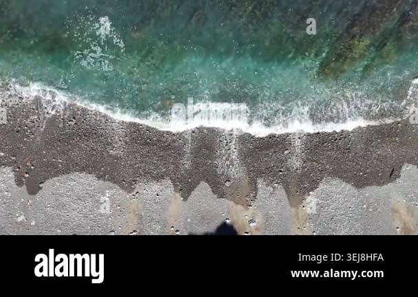 Top down aerial view with movement to the right of turquoise sea waves ...
