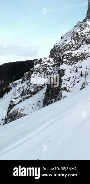 Narrow Snow Apron Beneath Towering Cliff, Tiny Skiers Descend Against ...