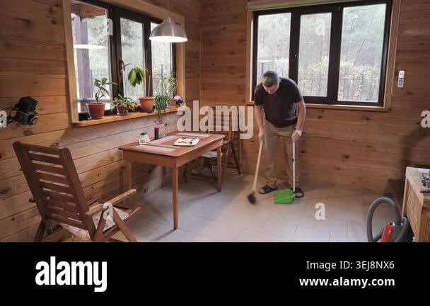 Man sweeping floor inside cozy wooden cabin during household cleaning ...