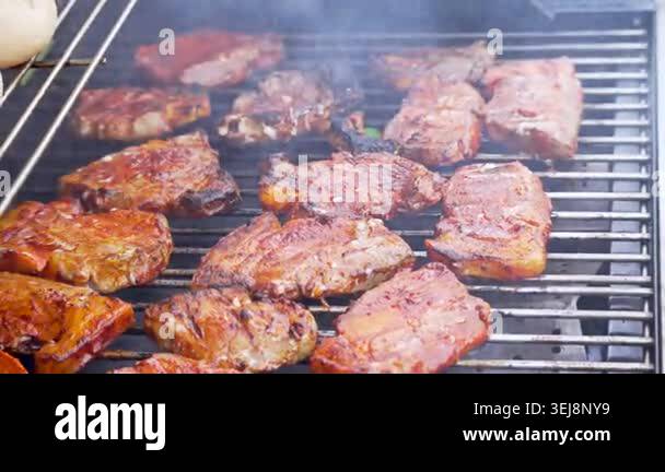 Pork steaks cook on an open grill under drifting smoke. Glossy marinade ...