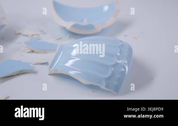 A blue ceramic piece lies broken on a white surface with small ...