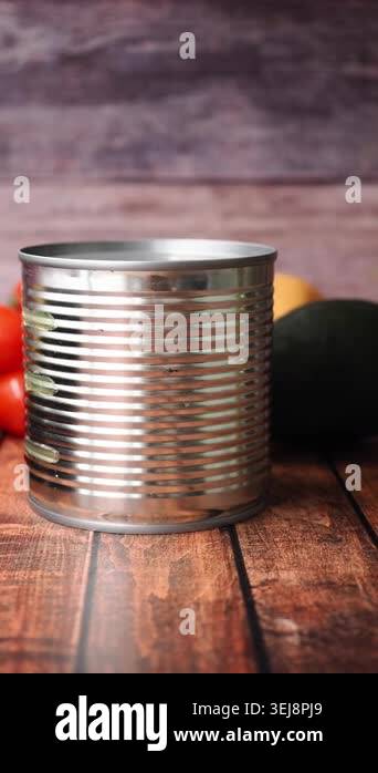 An empty can sits on a wooden table surrounded by fruits and vegetables ...