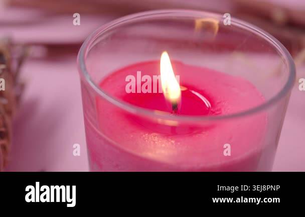 A pink candle is lit on a table, giving light and warmth to the space ...