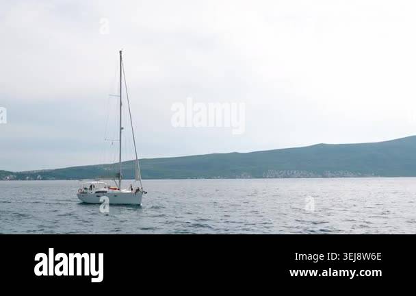 White sailboat cruising near coastline, small crew onboard, gentle ...