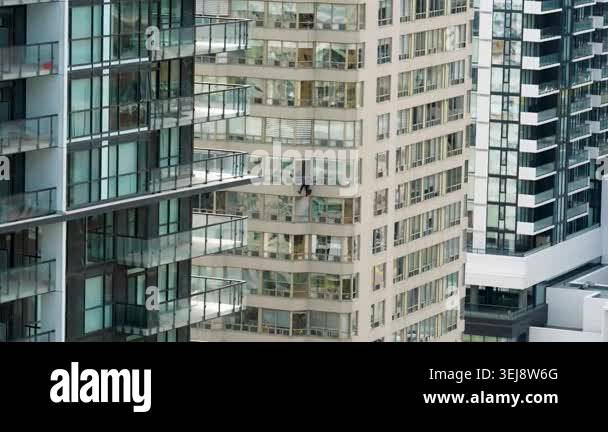 Cinematic urban footage of a window washer suspended by ropes while ...
