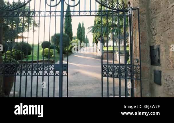 Wrought iron gate frames Italian villa. Sunlit cypresslined driveway ...