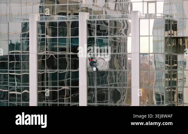 Highrise cleaner polishing mirrored glass with coordinated rope access ...