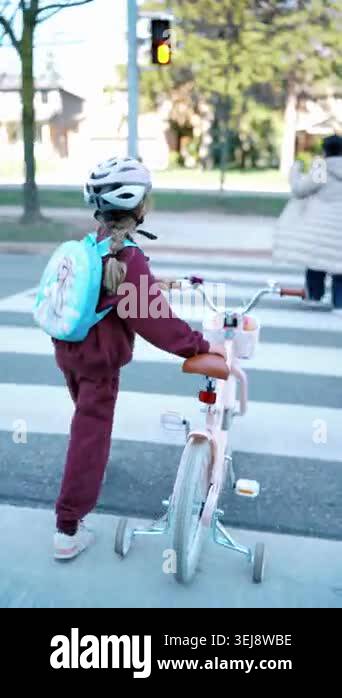 Asian girl pushes bike across crosswalk near suburban street with adult ...