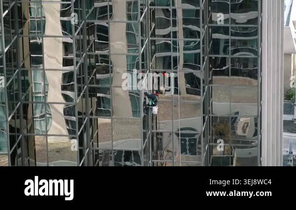 Rope technician navigating narrow facade gap cleaning glass wall ...