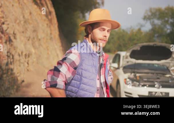 white man stranded beside broken car on sunlit rural road, hood open ...