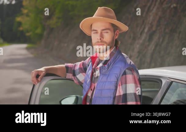white man smiling beside repaired car on quiet country road, leaning on ...