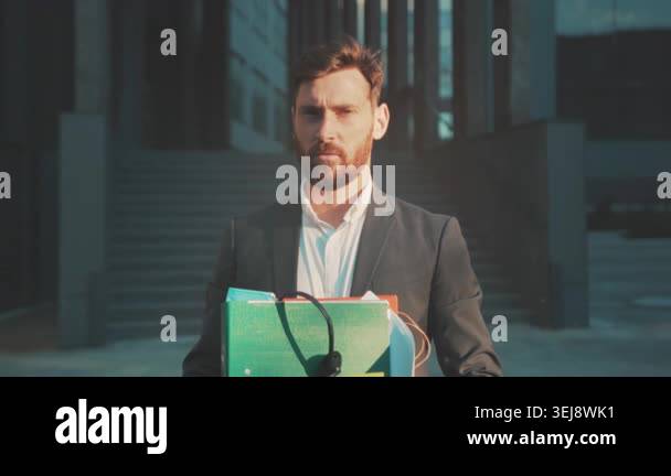 white executive stares into camera holding green folder box at building ...