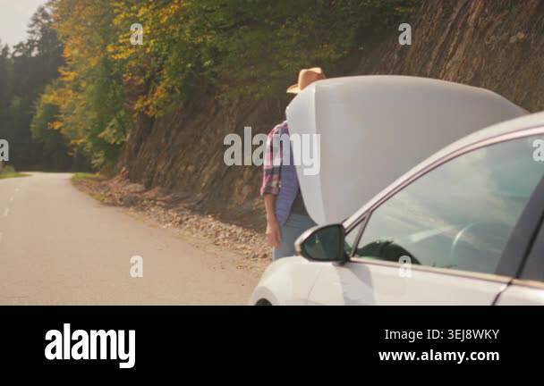White man stranded beside rural road with open hood hands on hips ...