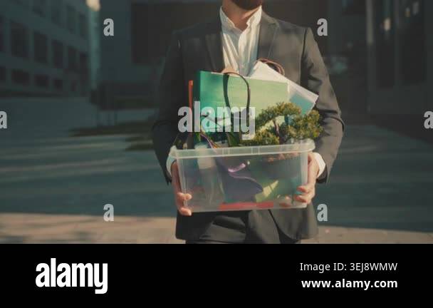 caucasian executive carrying box outside office building, slow walk ...