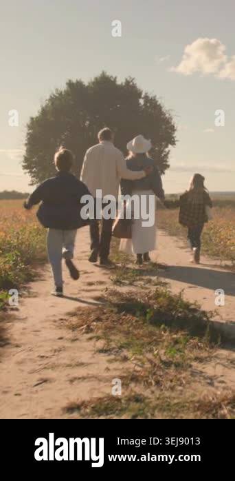 family walking down sunlit dirt path toward lone tree, parents holding ...