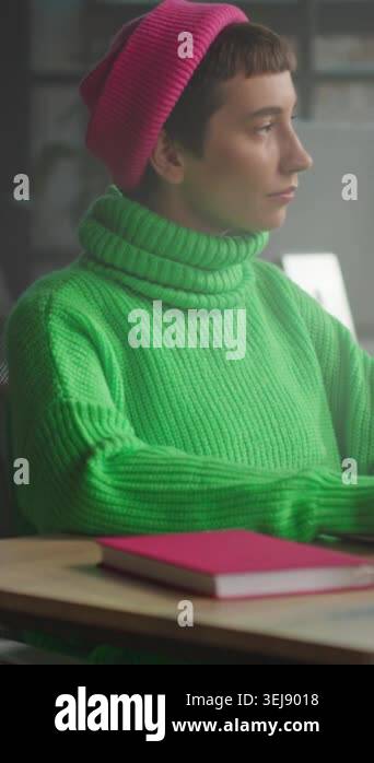 young adult at cafe table typing on laptop, neon green sweater and pink ...