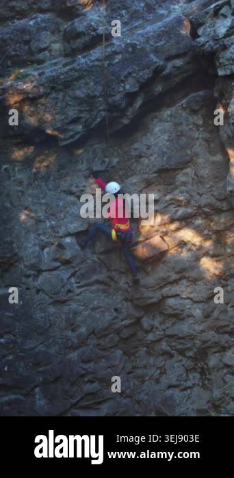 unspecified female climber on sunlit rock, red jacket and white helmet ...