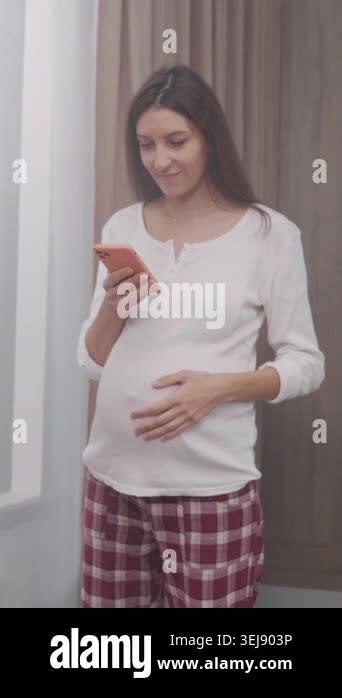 pregnant white woman checking phone and smiling while holding bump ...