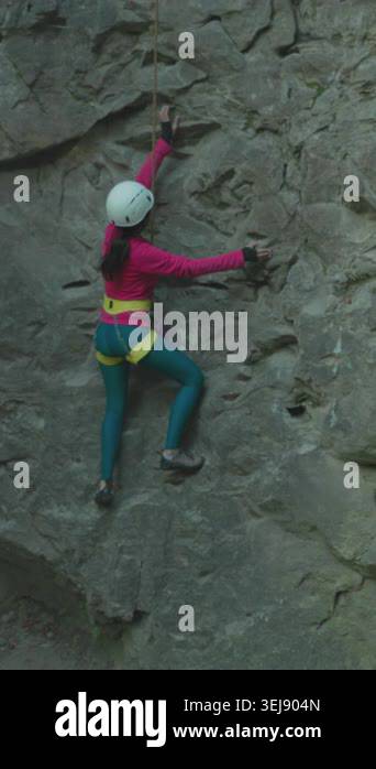 female climber scaling steep limestone wall wearing pink jacket and ...