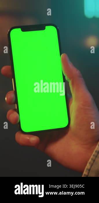 Hand holding smartphone green screen, warm neon bokeh background ...