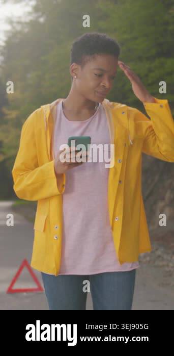 young woman in yellow raincoat waiting roadside with phone, looking ...