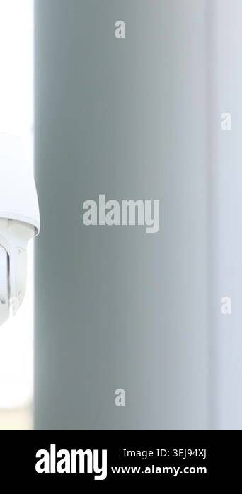 White outdoor security camera on building with green branches closeup ...